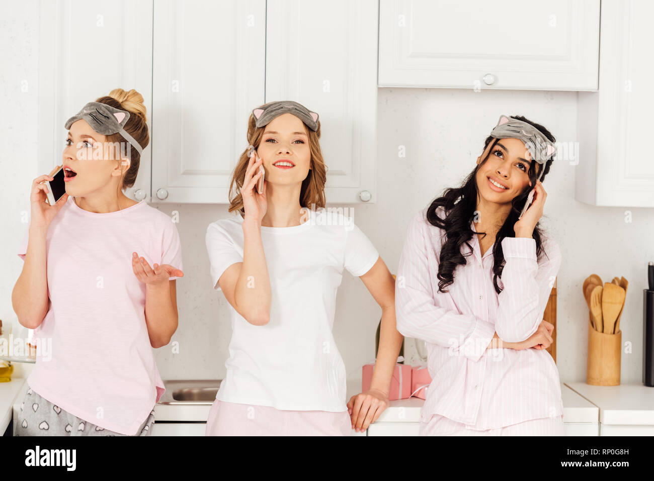 beautiful multicultural girls in sleeping masks talking on smartphones ...