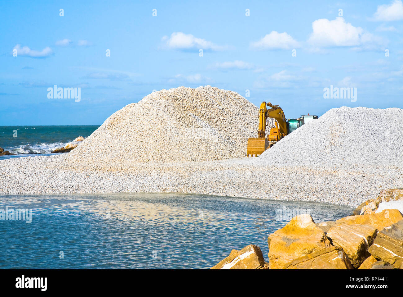Diggers on the seashore building a breakwater Stock Photo - Alamy