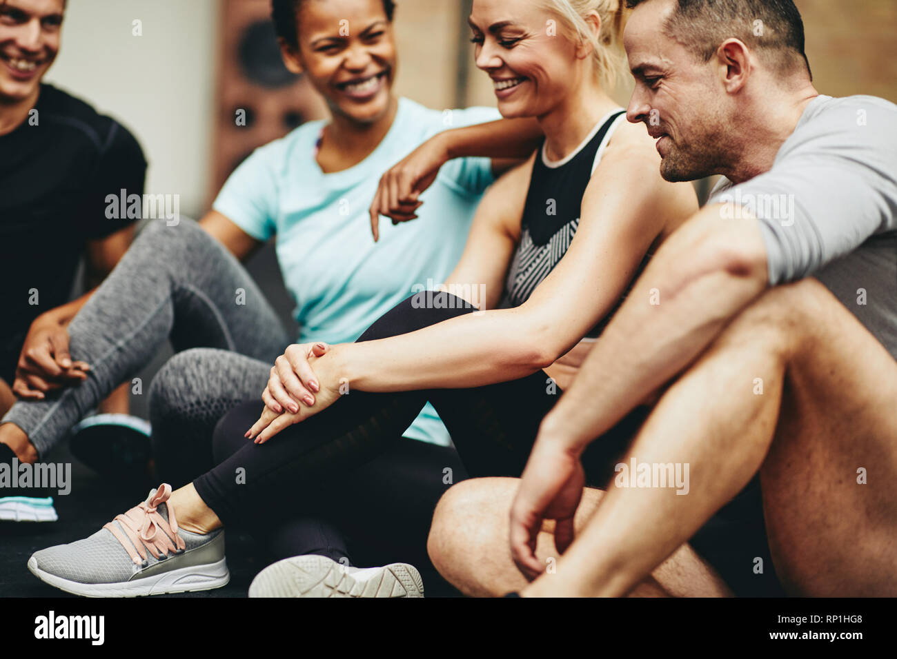 Group of diverse friends in sportswear laughing while sitting on a gym ...