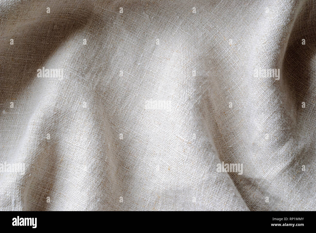 Soft folds of a natural woven linen fabric in close up detail in a full ...