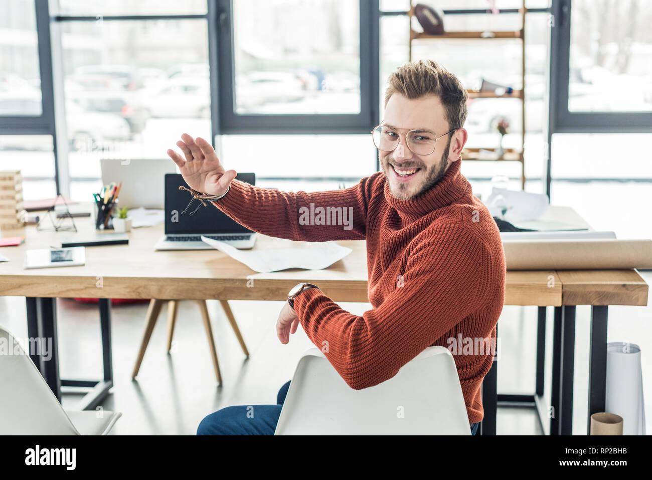 male architect sitting at computer desk, waving and working on ...