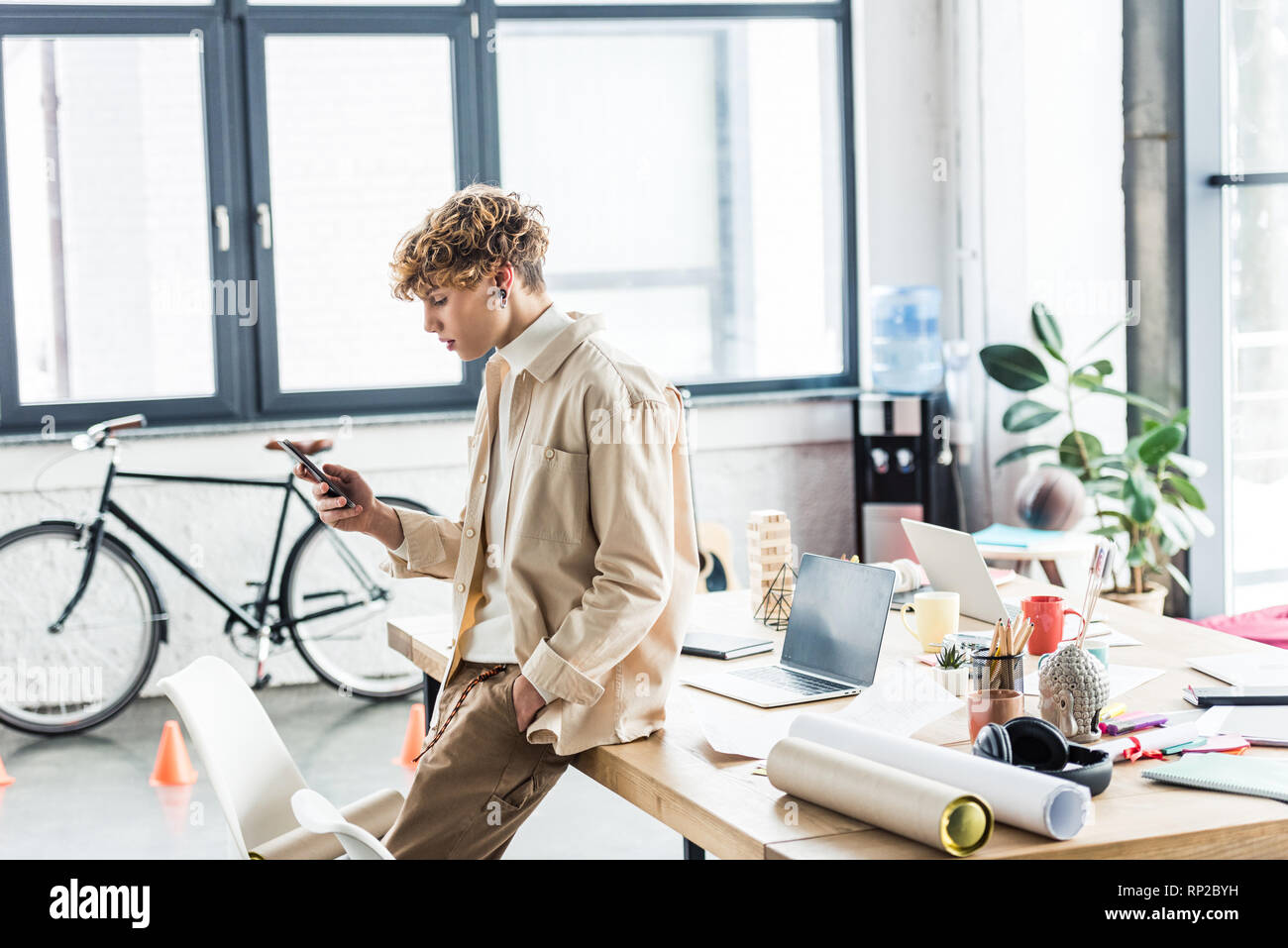 handsome architect using smartphone near table with blueprints in loft ...
