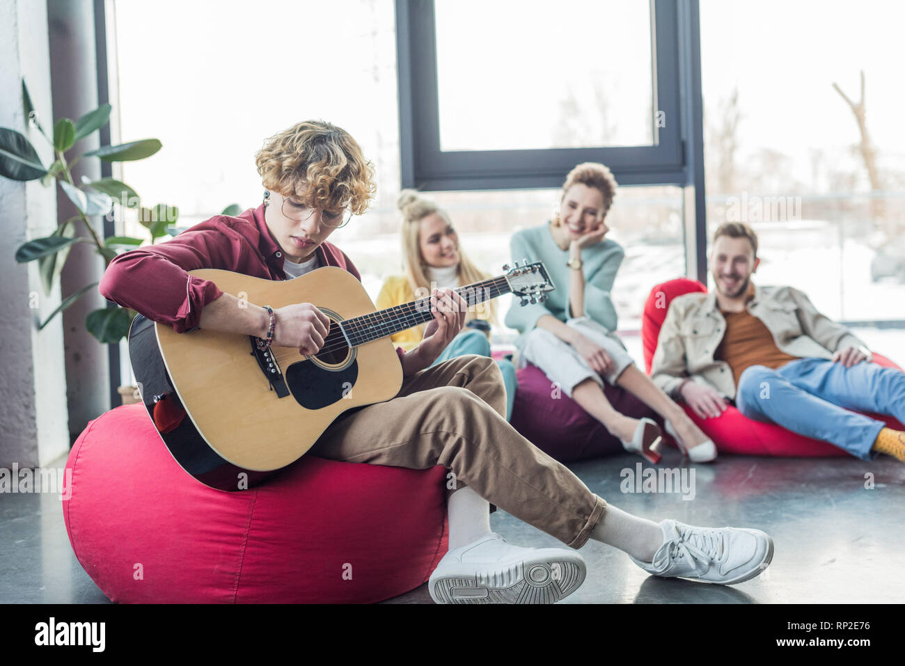 group of friends sitting on bean bag chairs and playing guitar Stock ...