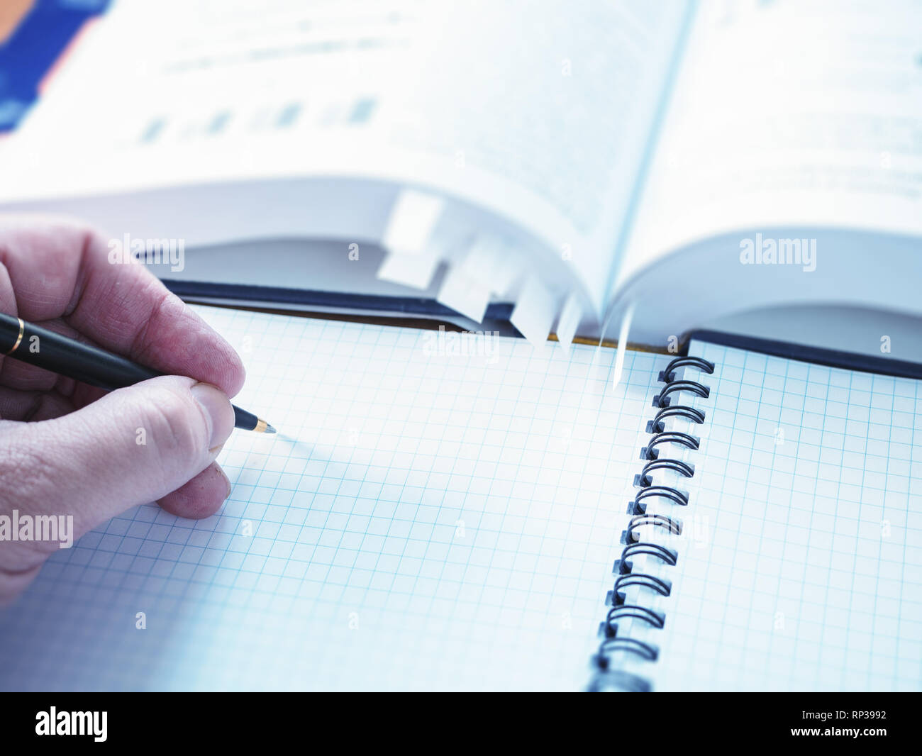 left handed man with pen witing notes at notebook while studying at ...