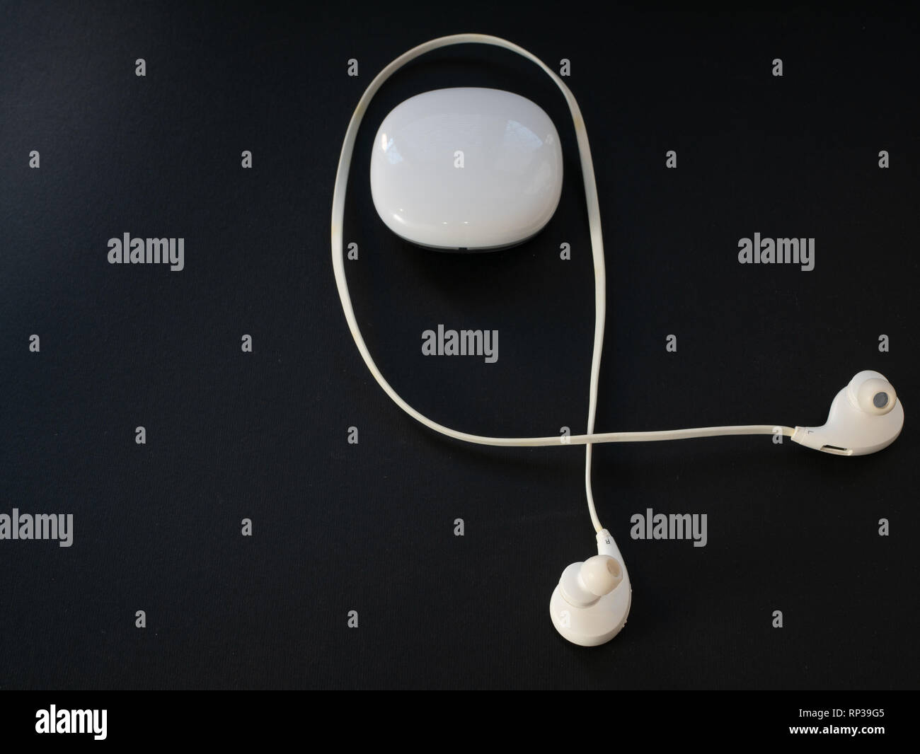 small white wireless earbuds with plastic box on black background ...