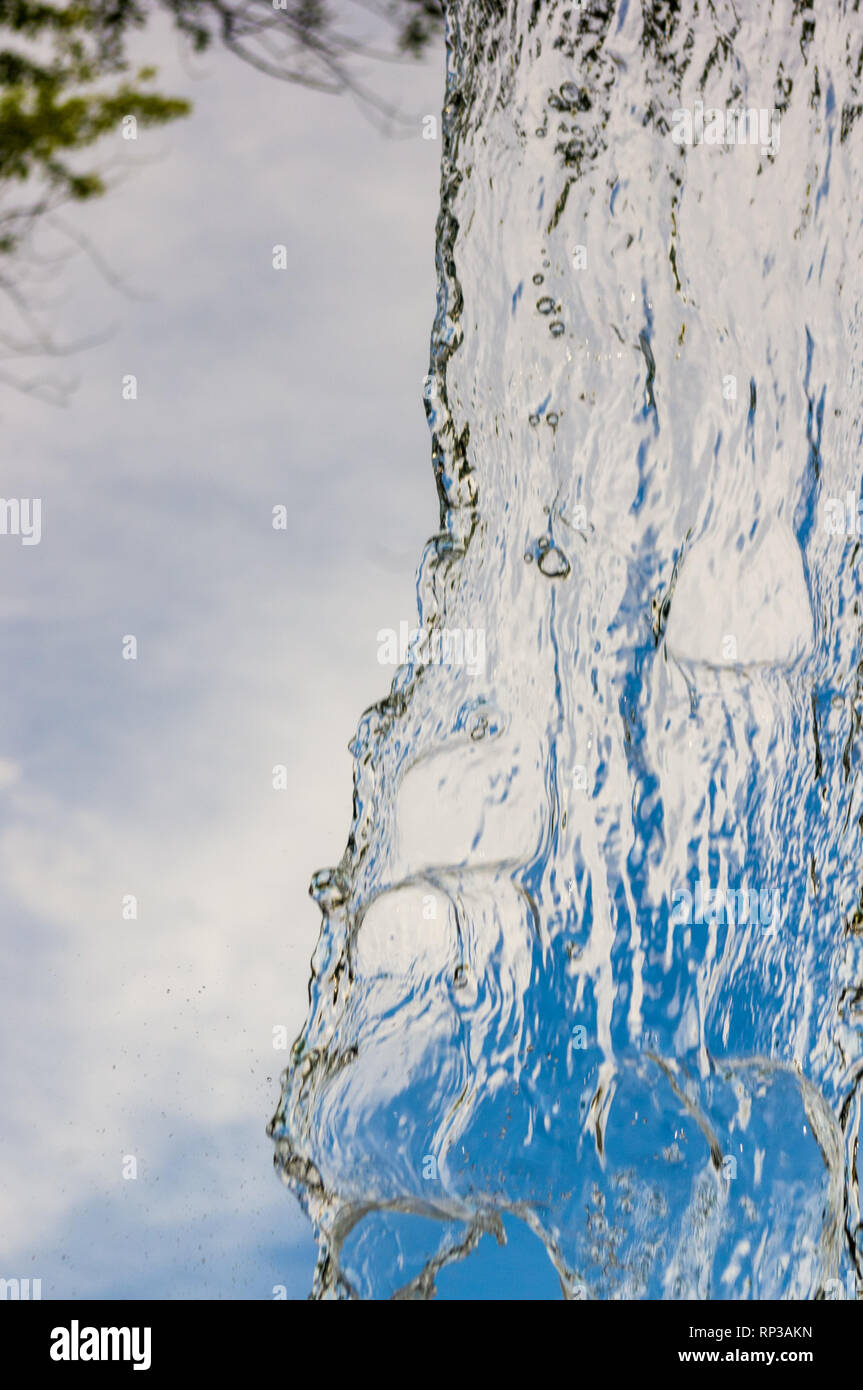 transparent falling water vertical flows against a blue sky and green ...