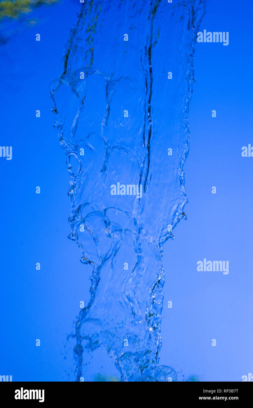 transparent falling water vertical flows against a blue sky and green ...