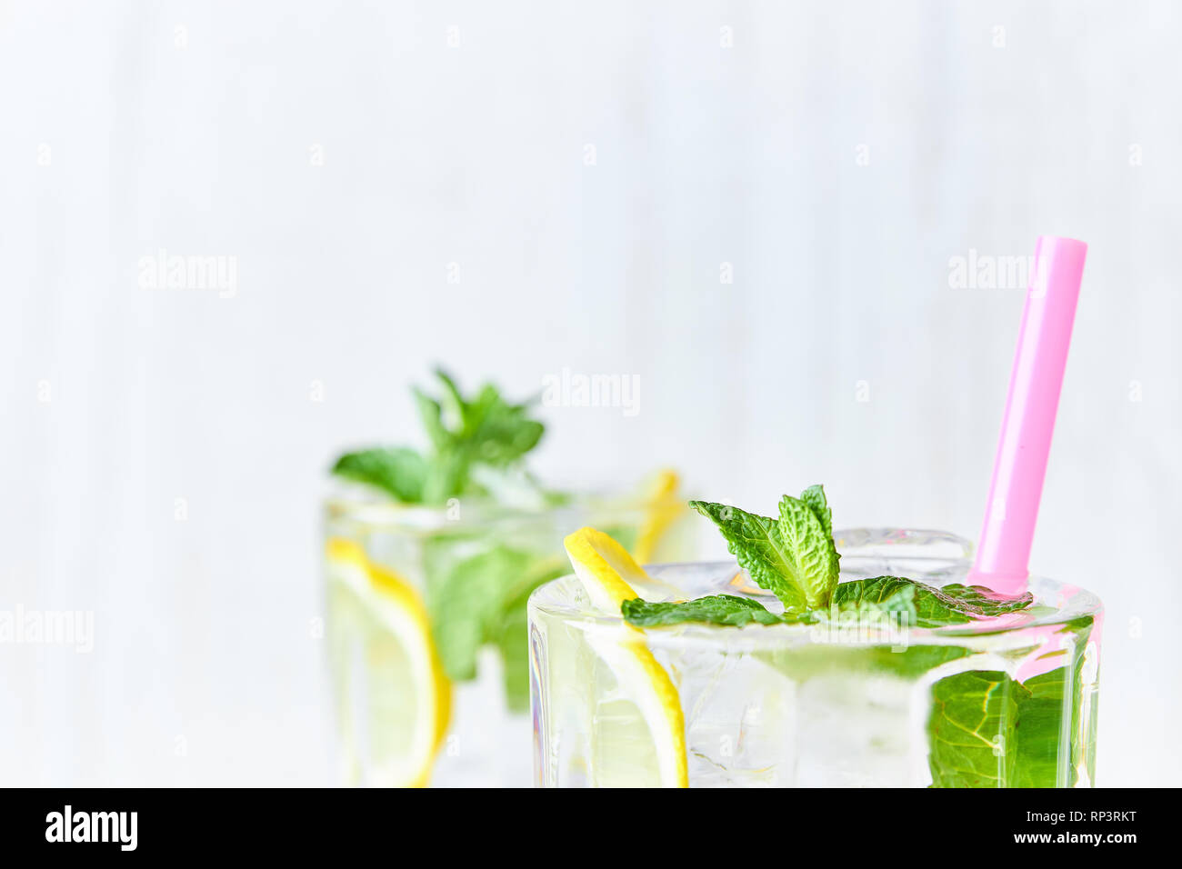 Lemonade with ice, lemon slices and mint in a glass with straw on a light wooden background ...
