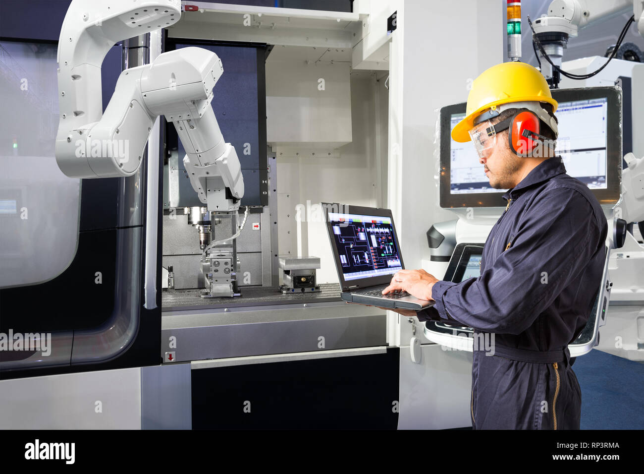 Maintenance engineer using laptop computer control automatic robotic hand with CNC machine in ...