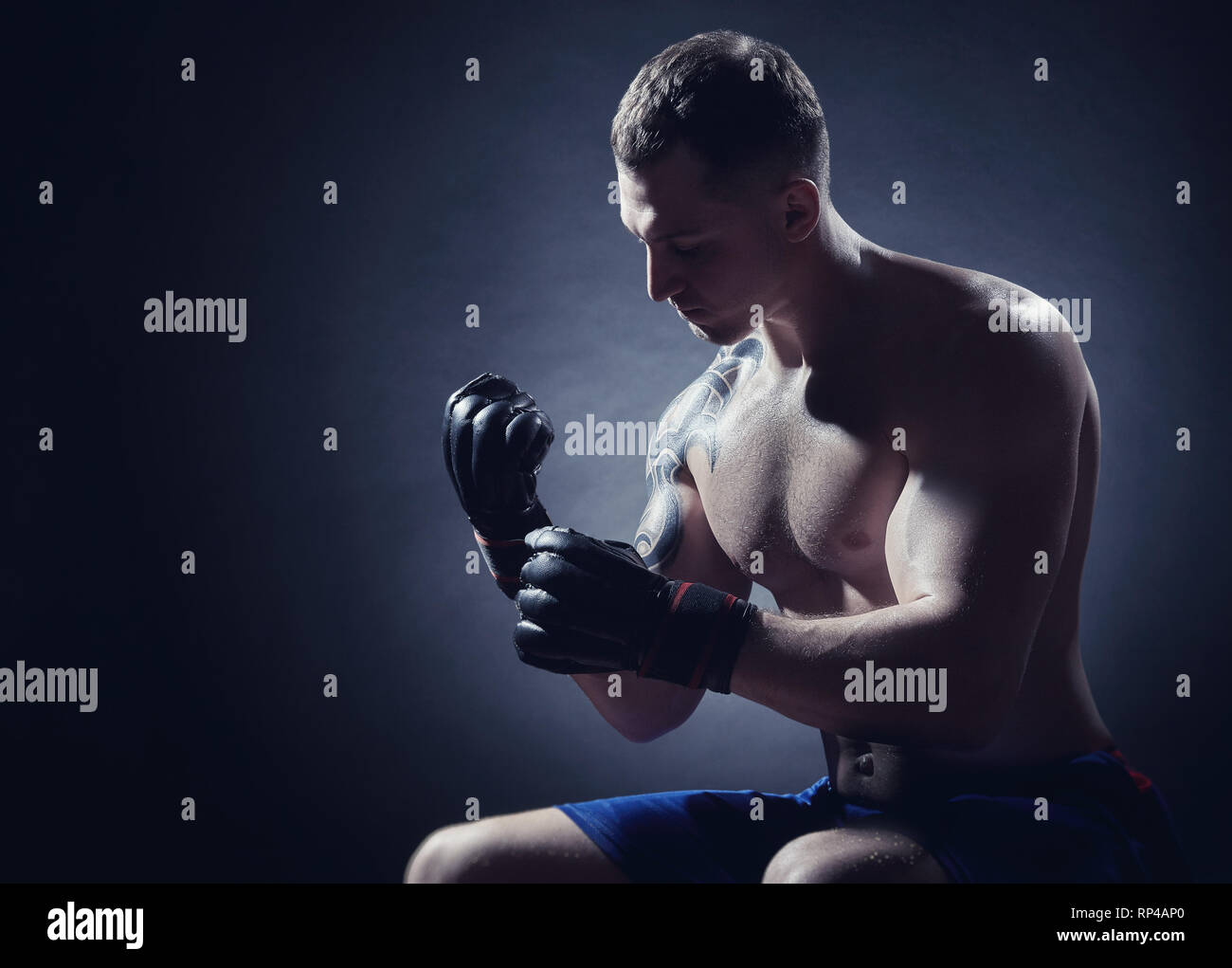 Boxer with boxing gloves sits before fight on a black background ...
