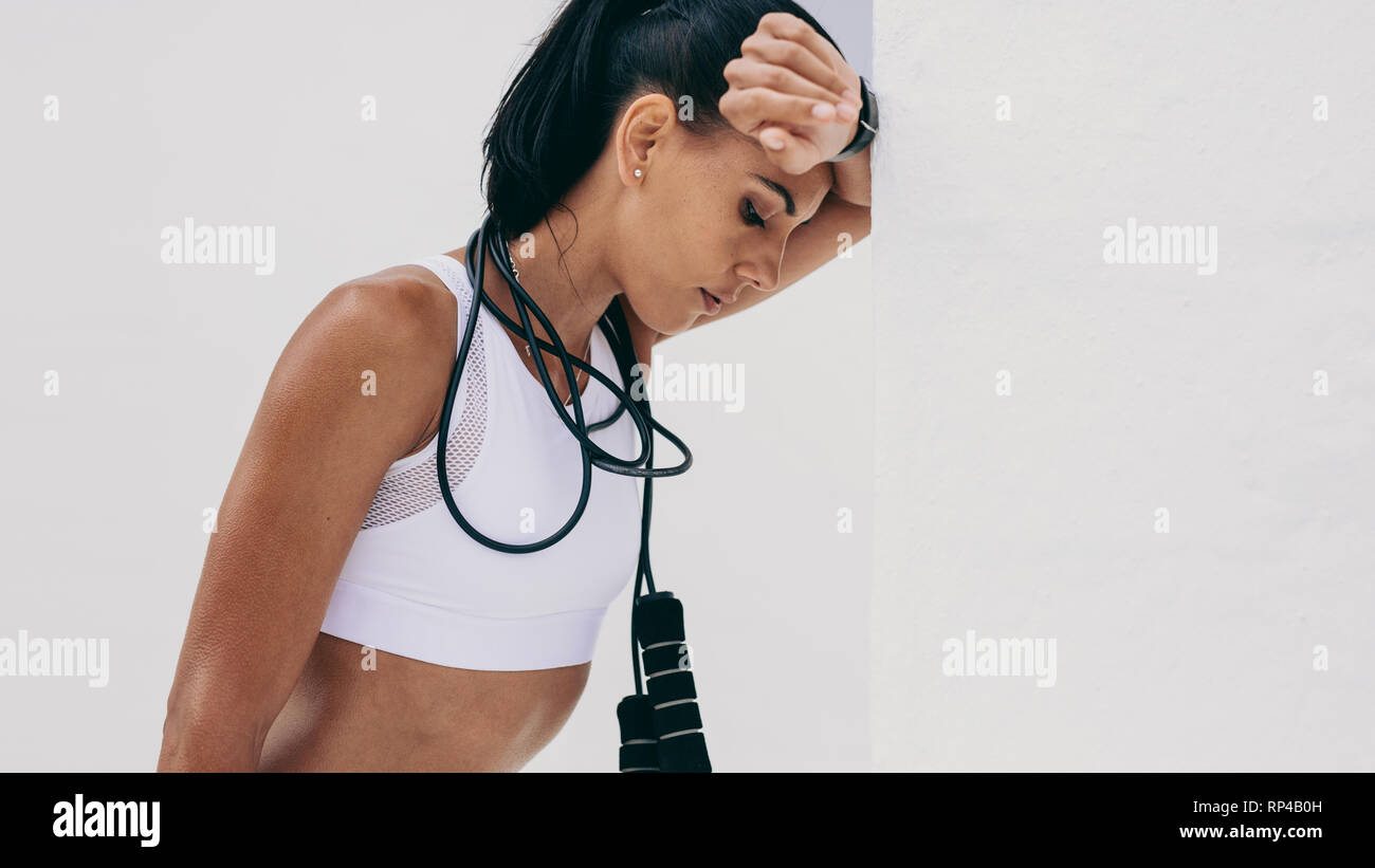 Woman in fitness wear resting her head on a wall with a skipping rope ...