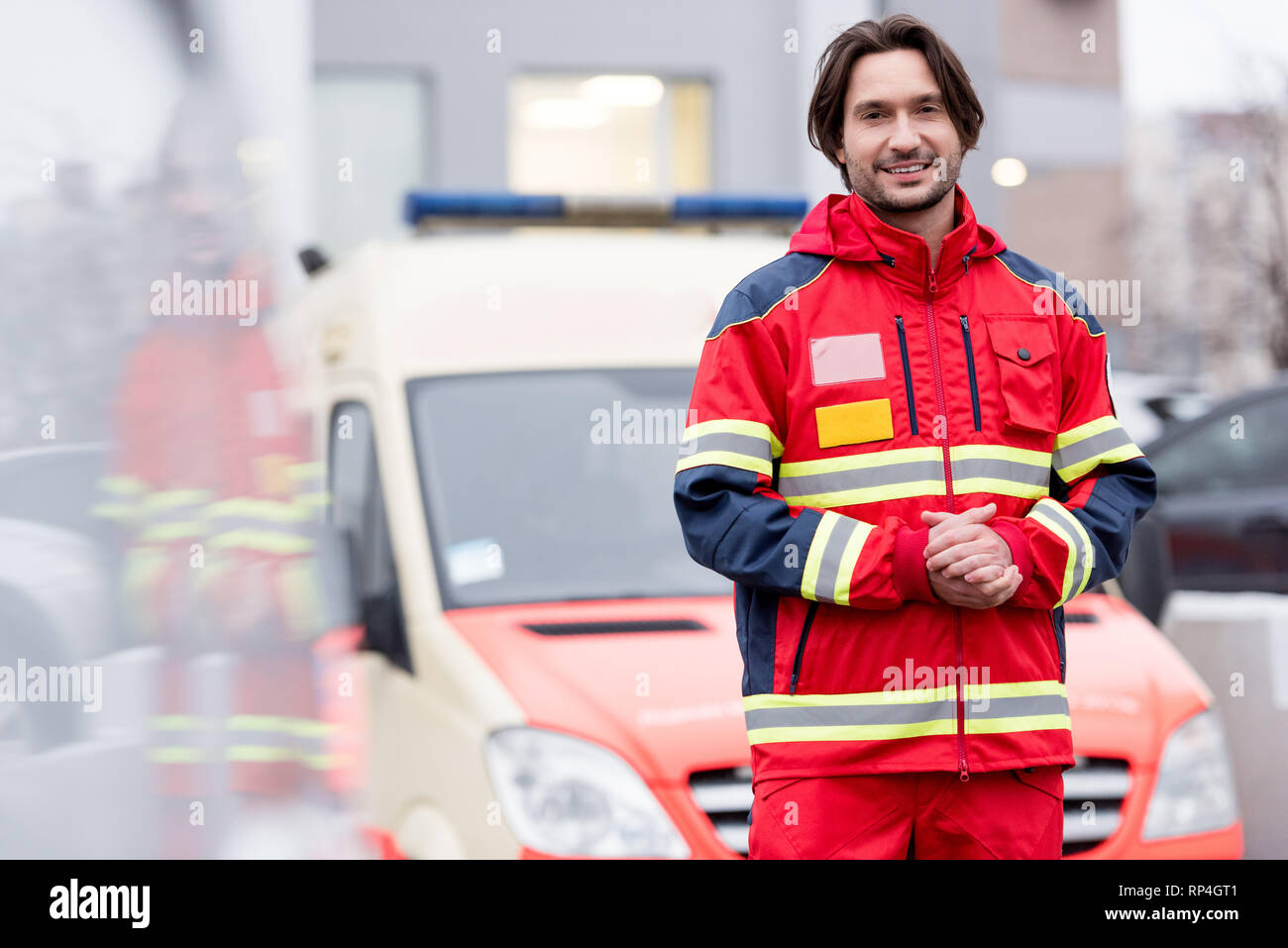 Smiling paramedic in uniform standing near ambulance car Stock Photo ...