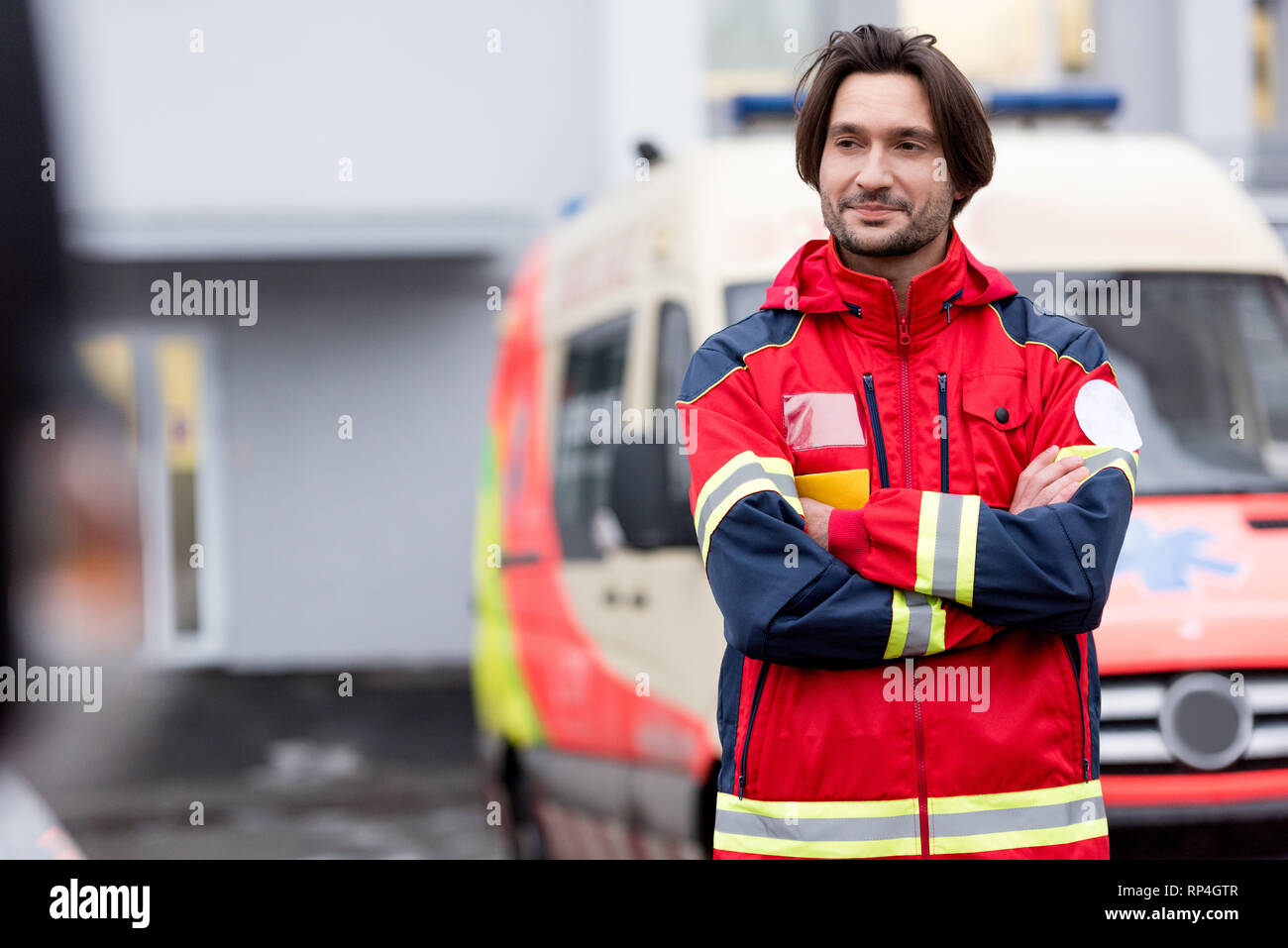 Confident paramedic in red uniform standing on street with crossed arms ...