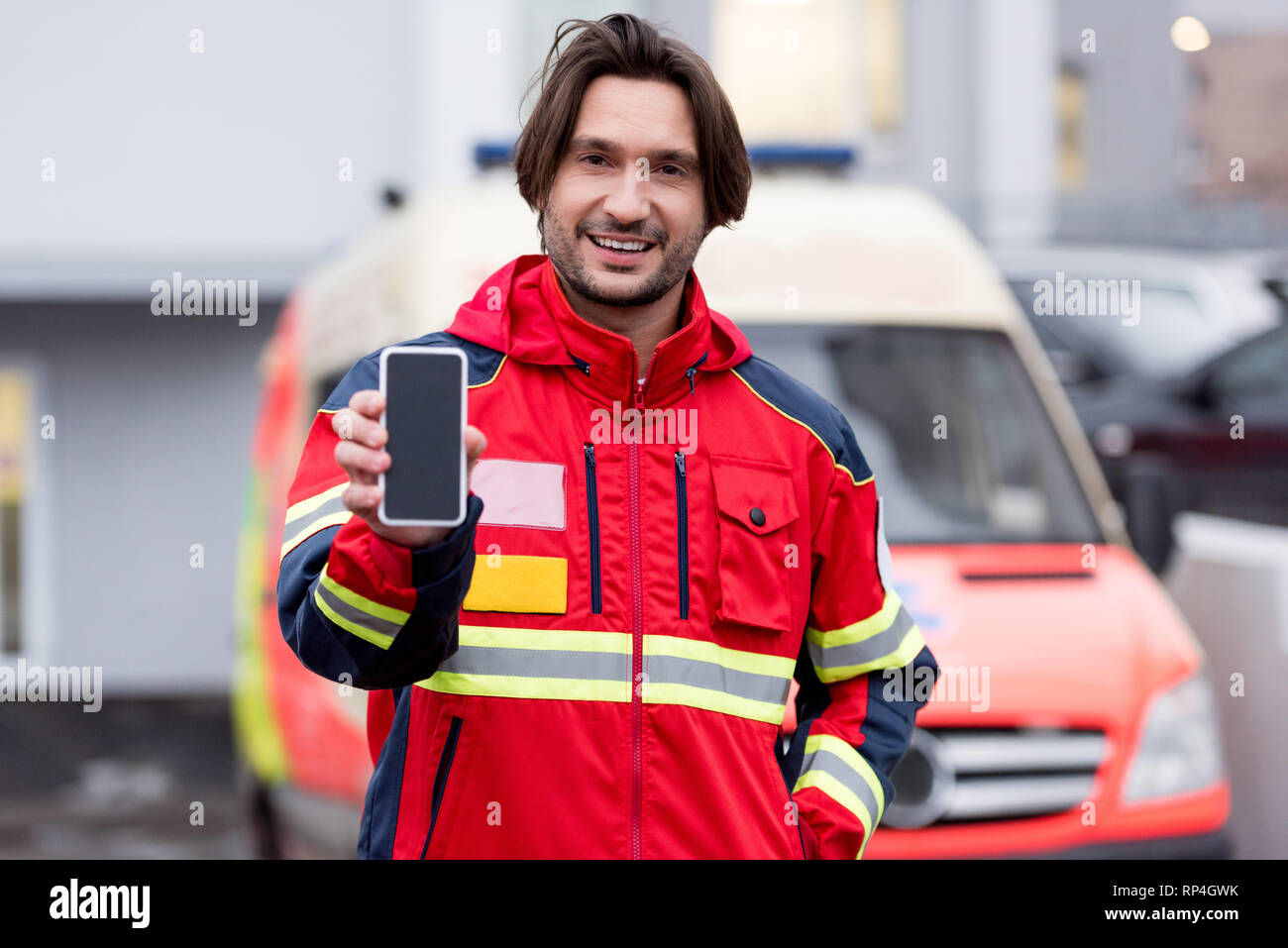 Smiling paramedic in red uniform holding smartphone with blank screen ...