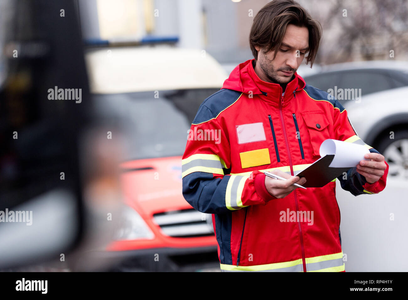 Concentrated paramedic in red uniform writing in clipboard Stock Photo ...