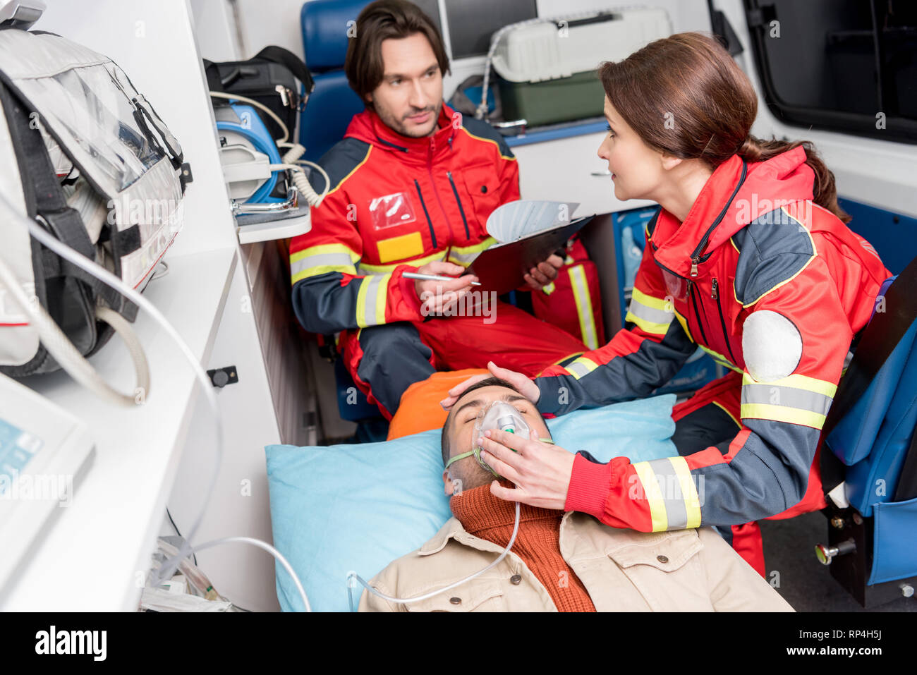 Female paramedic holding oxygen mask on patient while colleague writing ...