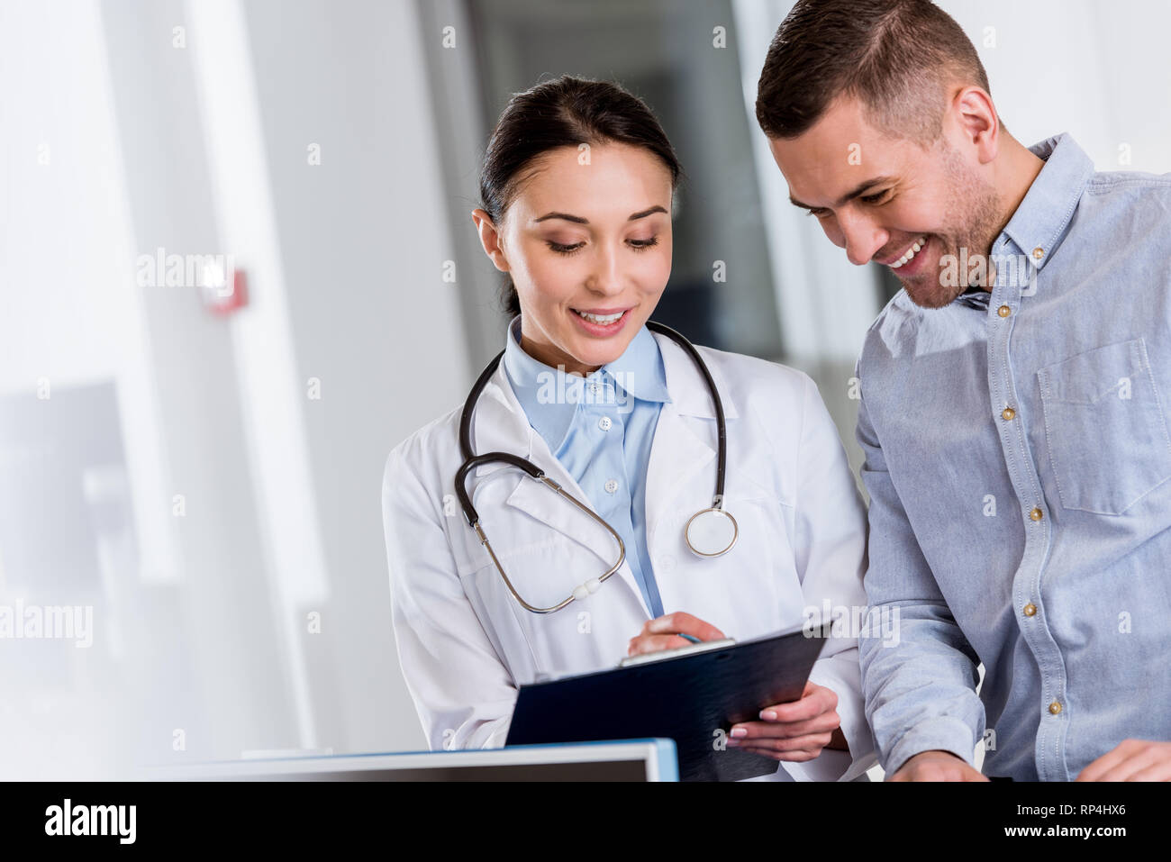 Laughing doctor talking to patient and writing in clipboard Stock Photo ...