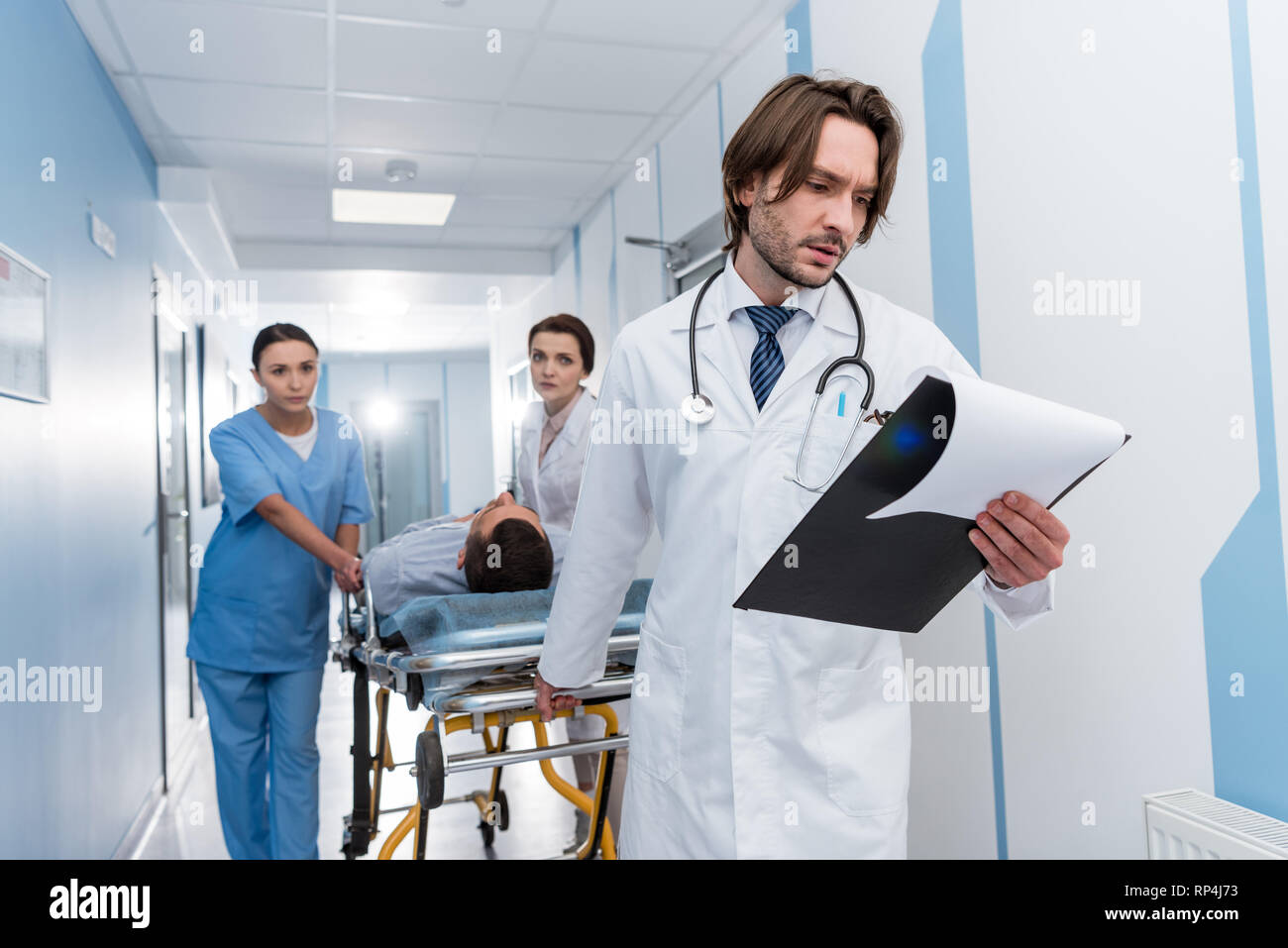 Doctor reading notes while colleagues transporting patient Stock Photo ...