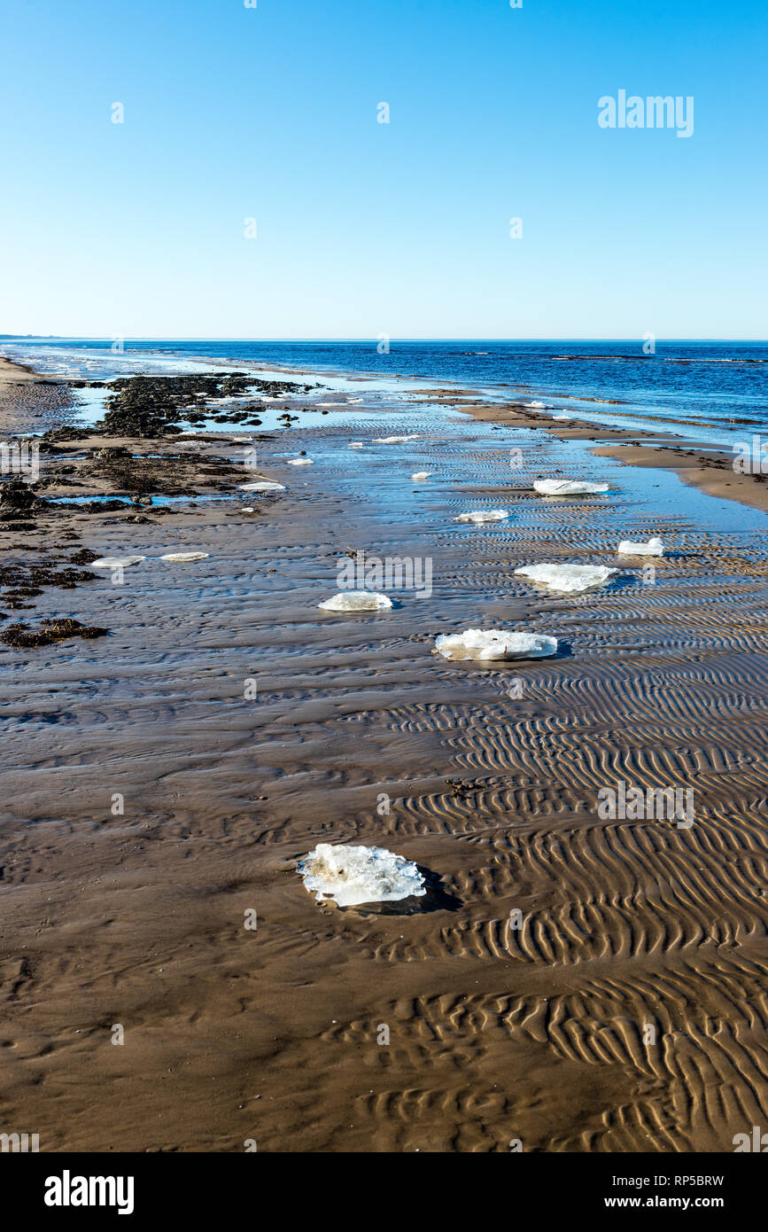 frozen ice blocks on sea beach in winter with sand and snow in overcast ...