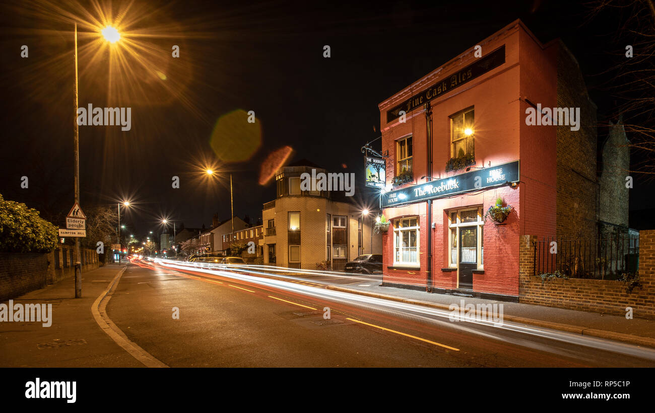 English pub at night on small road with long exposure traffic passing ...