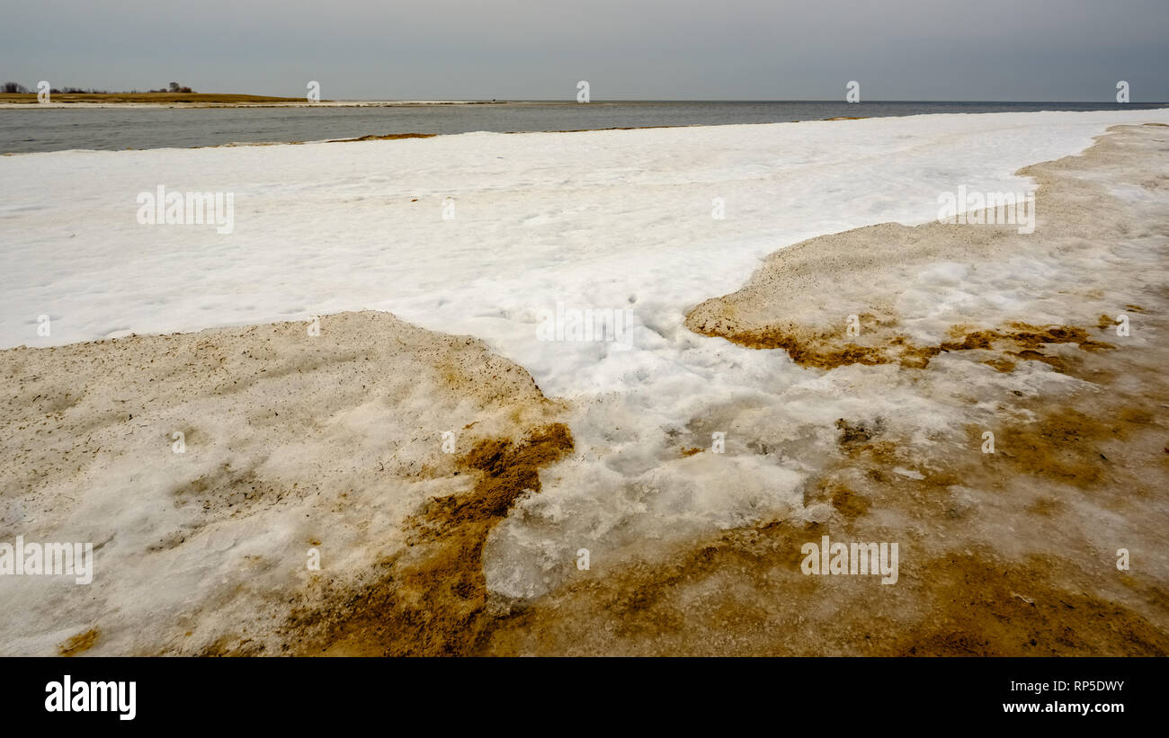 frozen ice blocks on sea beach in winter with sand and snow in overcast ...