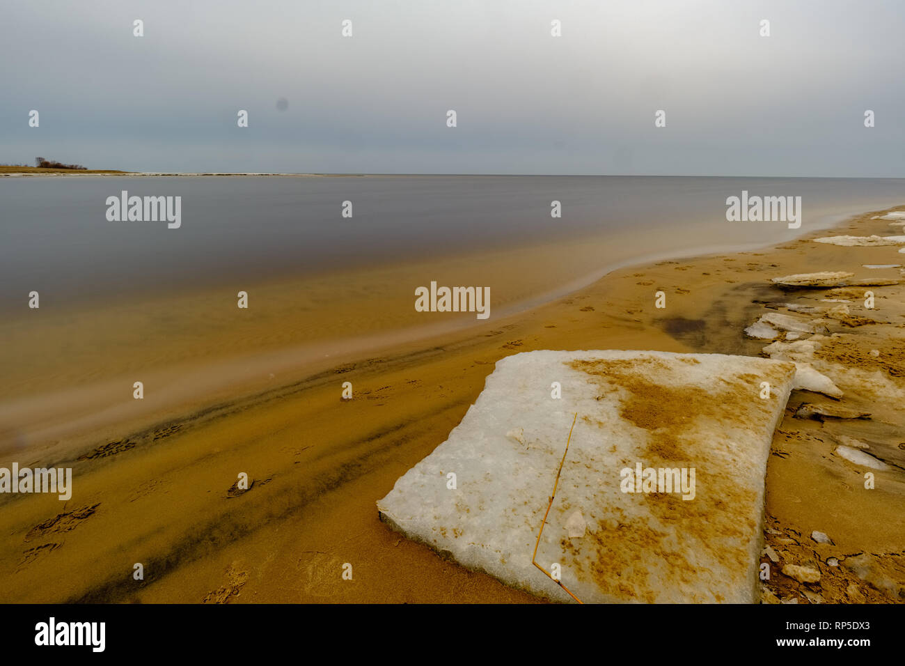 frozen ice blocks on sea beach in winter with sand and snow in overcast ...