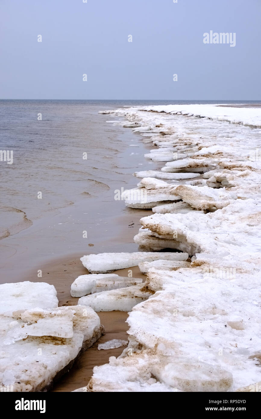 frozen ice blocks on sea beach in winter with sand and snow in overcast ...
