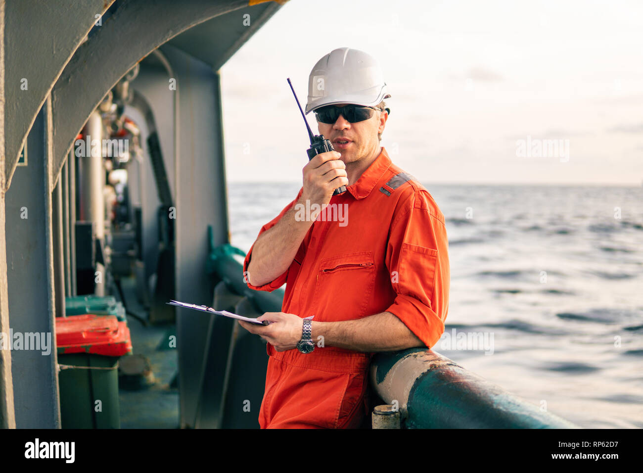 Deck Officer on deck of offshore vessel holds VHF walkie-talkie radio ...