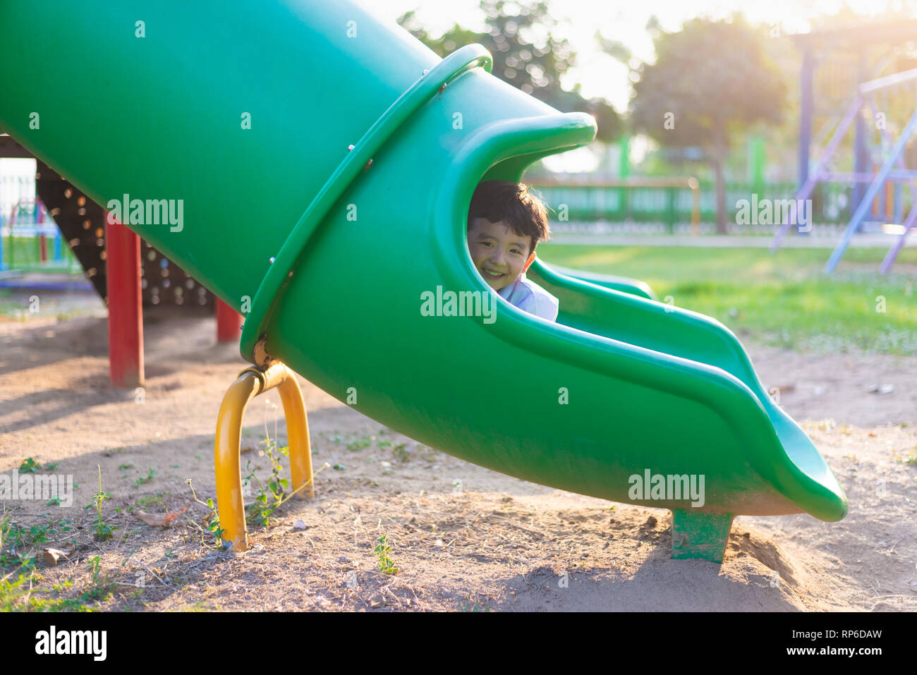 Asian kid playing slide at the playground under the sunlight in summer ...