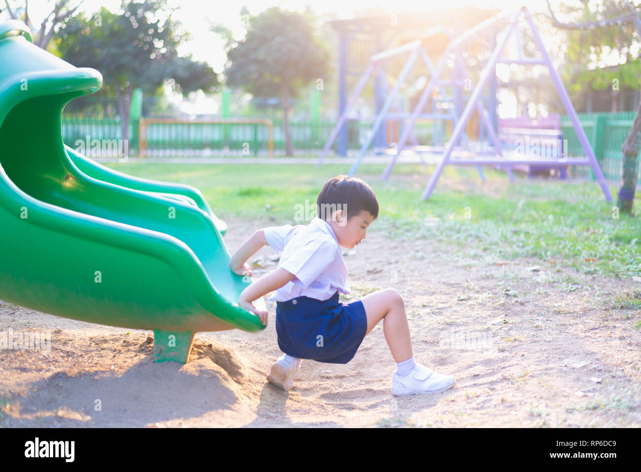 Asian kid playing slide at the playground under the sunlight in summer ...