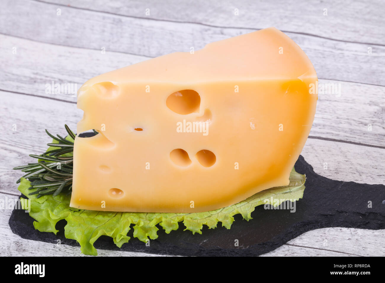 Maasdam cheese on the board served salad leaves and rosemary Stock ...