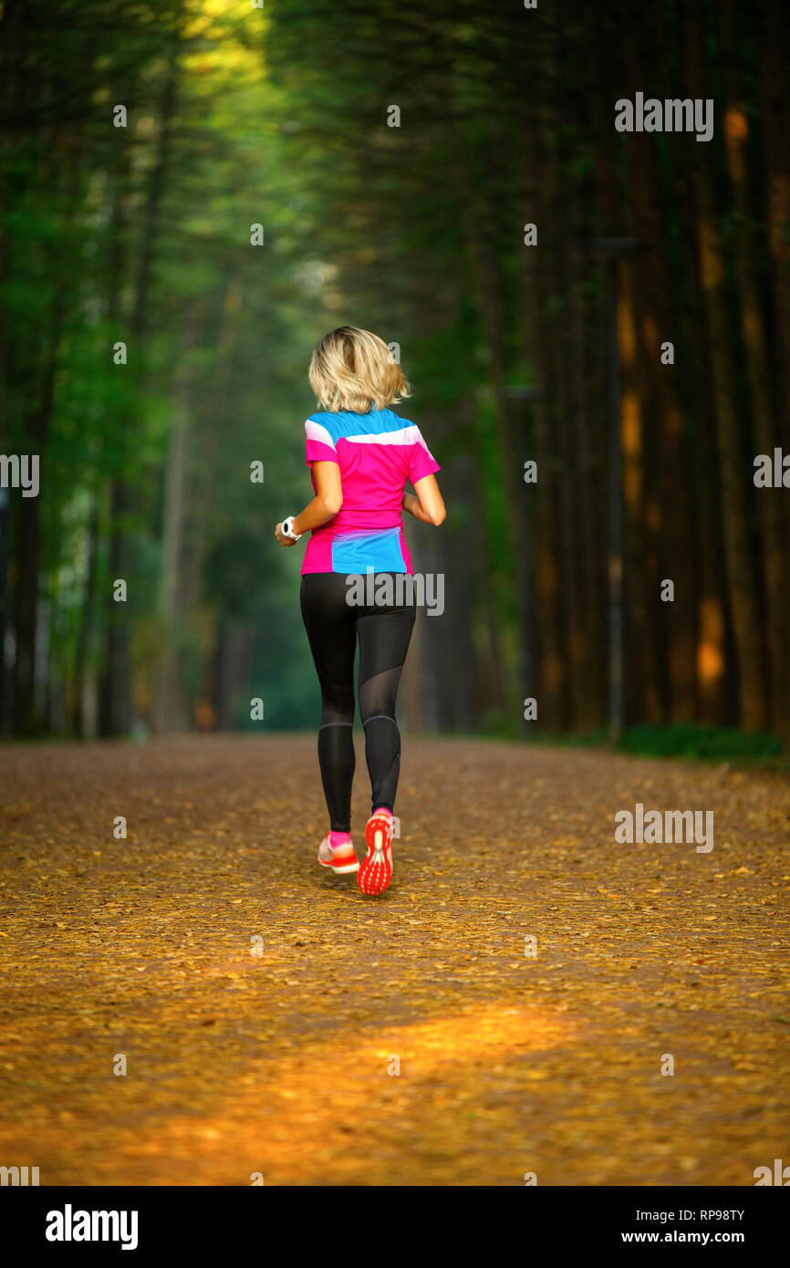 Photo from back of sports woman running through park among trees on ...