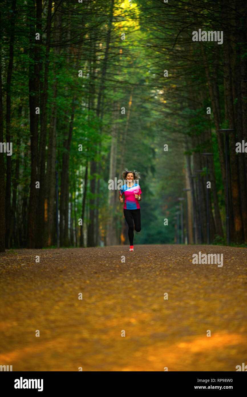 Photo from back of sports woman running through park among trees on ...