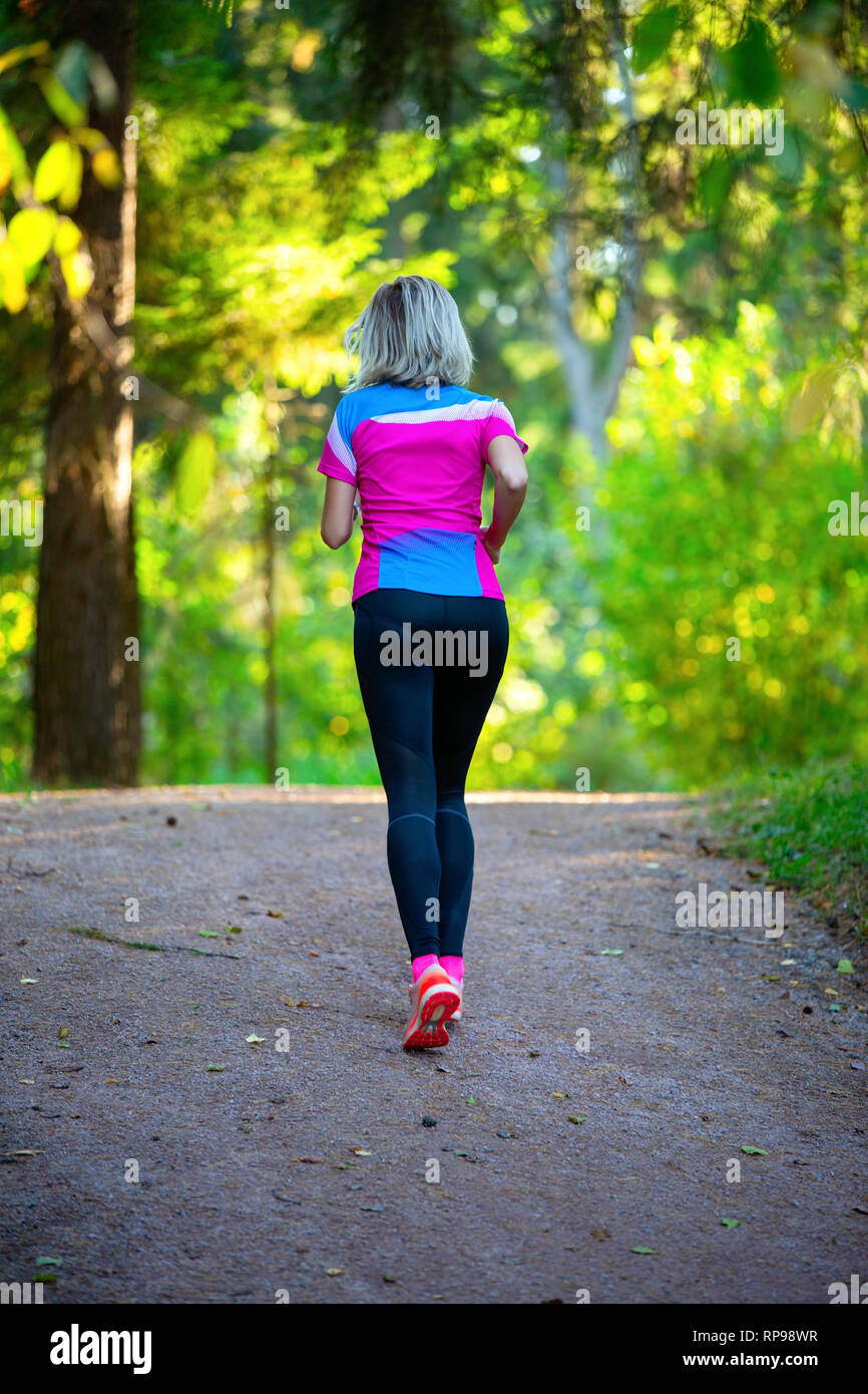 Photo from back of blonde athlete woman running through park among ...