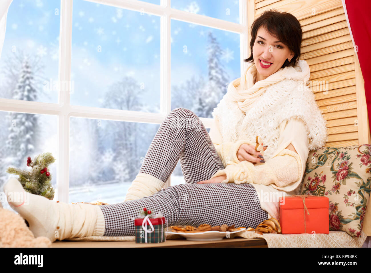 Woman is sitting on a window sill and showing a cookie angel. Beautiful ...