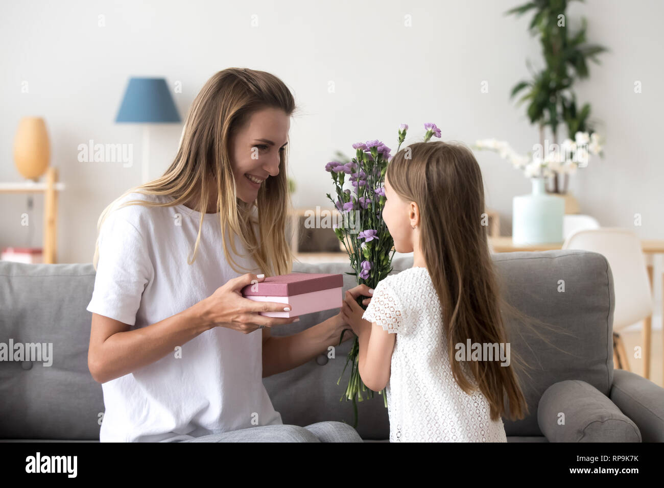 Excited mother receiving gift and flowers from little loving daughter ...