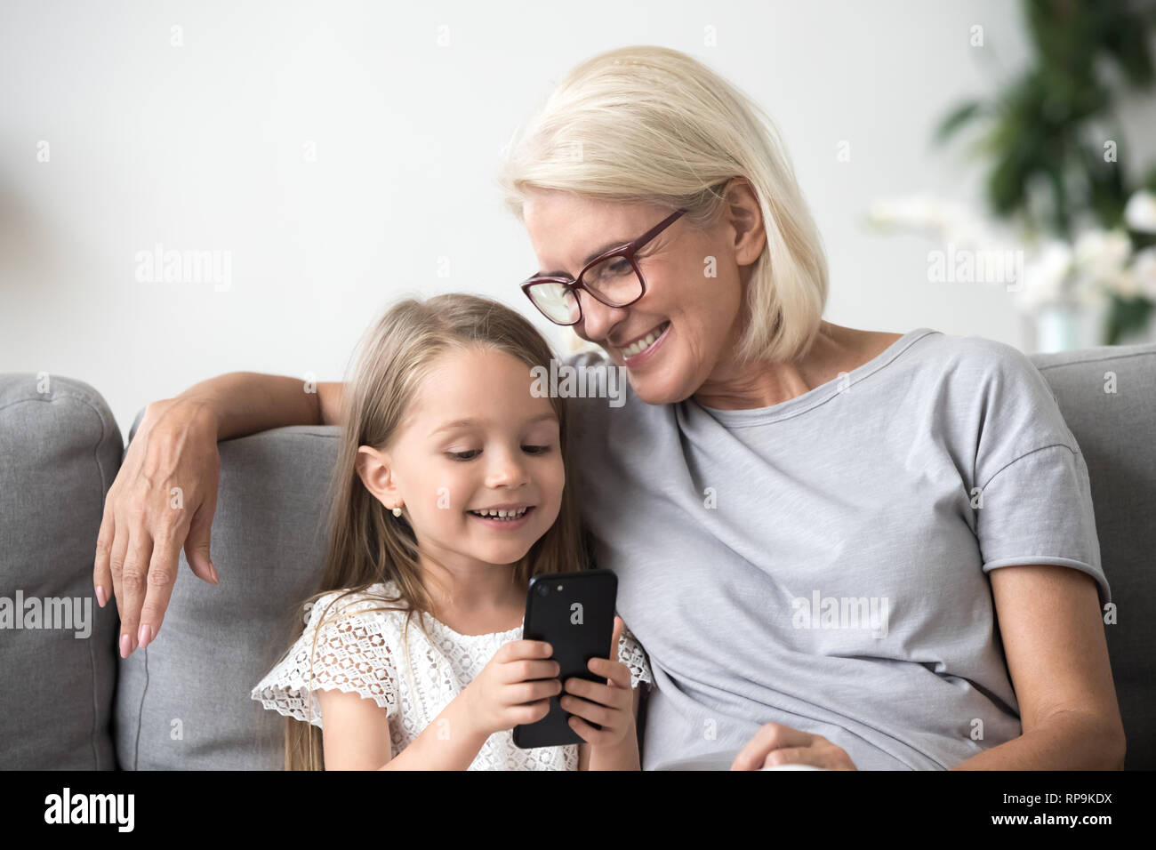 Happy Grandmother And Granddaughter Using Phone Together At Home Stock