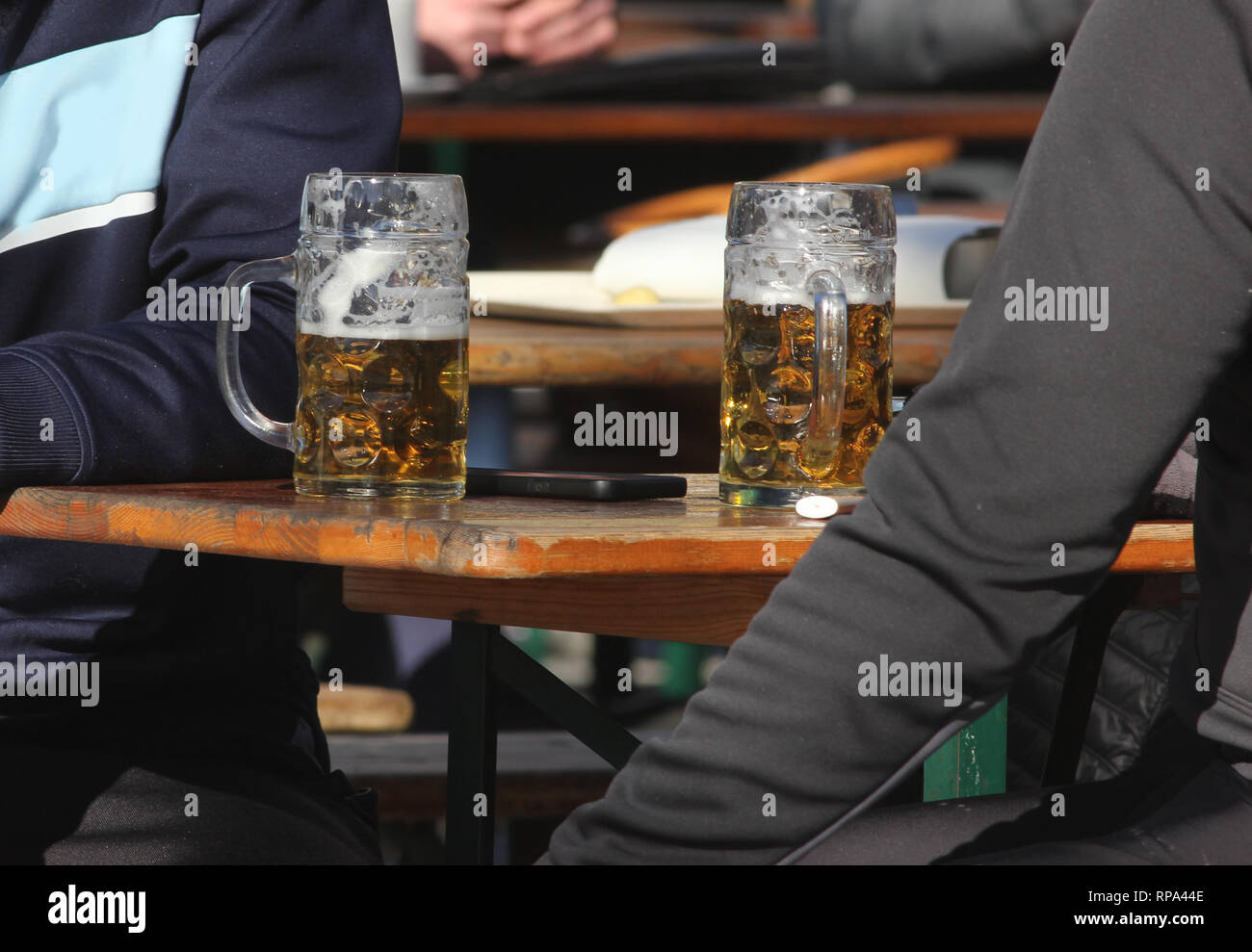 Guys with half drunken beers plus iphone on a beer garden table. Sun is ...