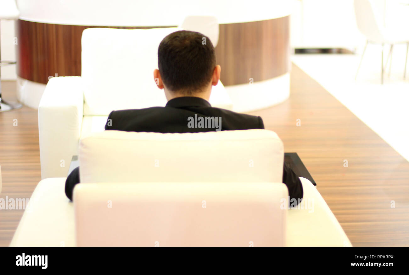 Picture of a man waiting from behind sitting on a white sofa in a hotel ...