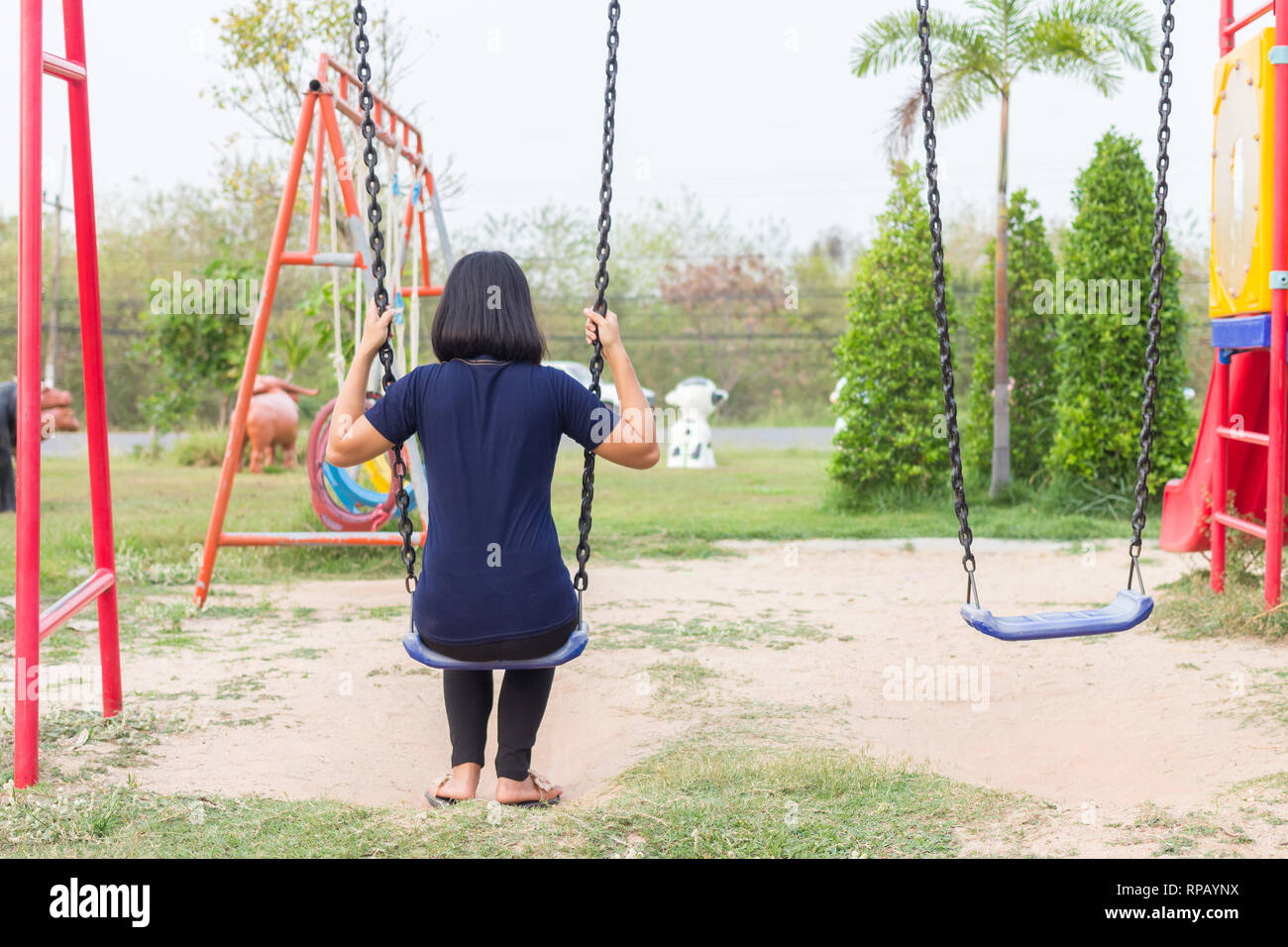 Woman sitting swing in playground Stock Photo - Alamy