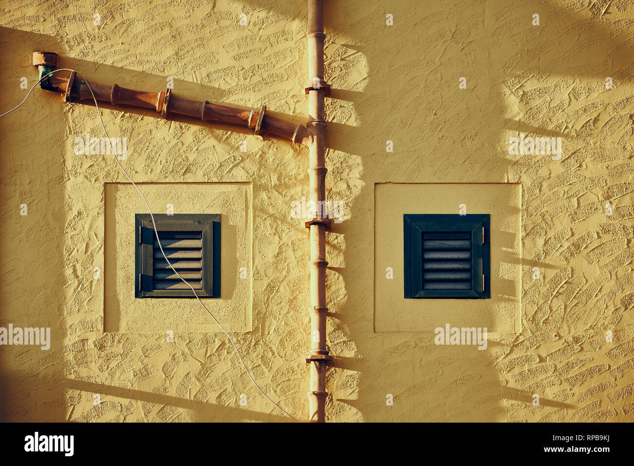 Yellow rugged wall with shutters and old ceramic gutter, color toned ...