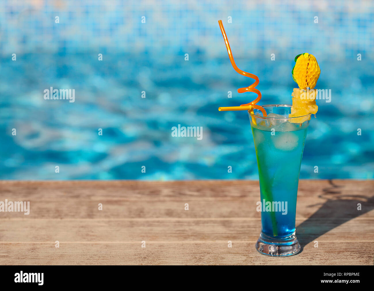 Glass with a bright blue lagoon cocktail on the table by the pool ...