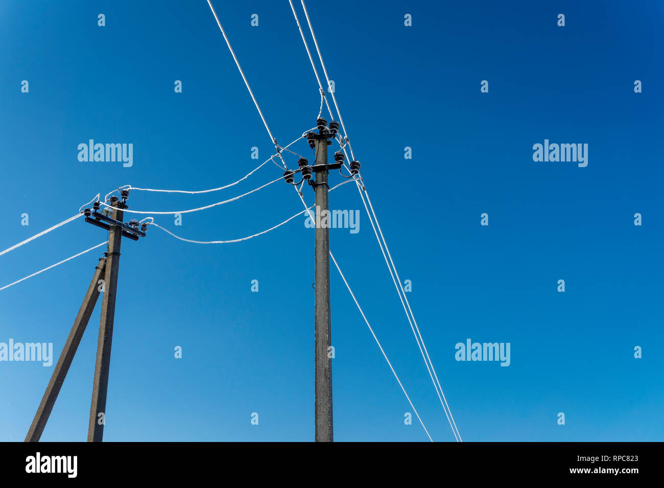 Two electric line poles with frozen wires in winter, viewed from low ...