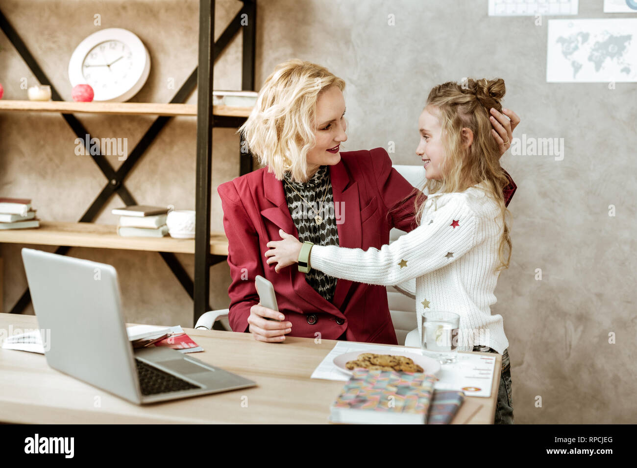 Long-haired cheerful little girl bringing cookies to her busy mother ...