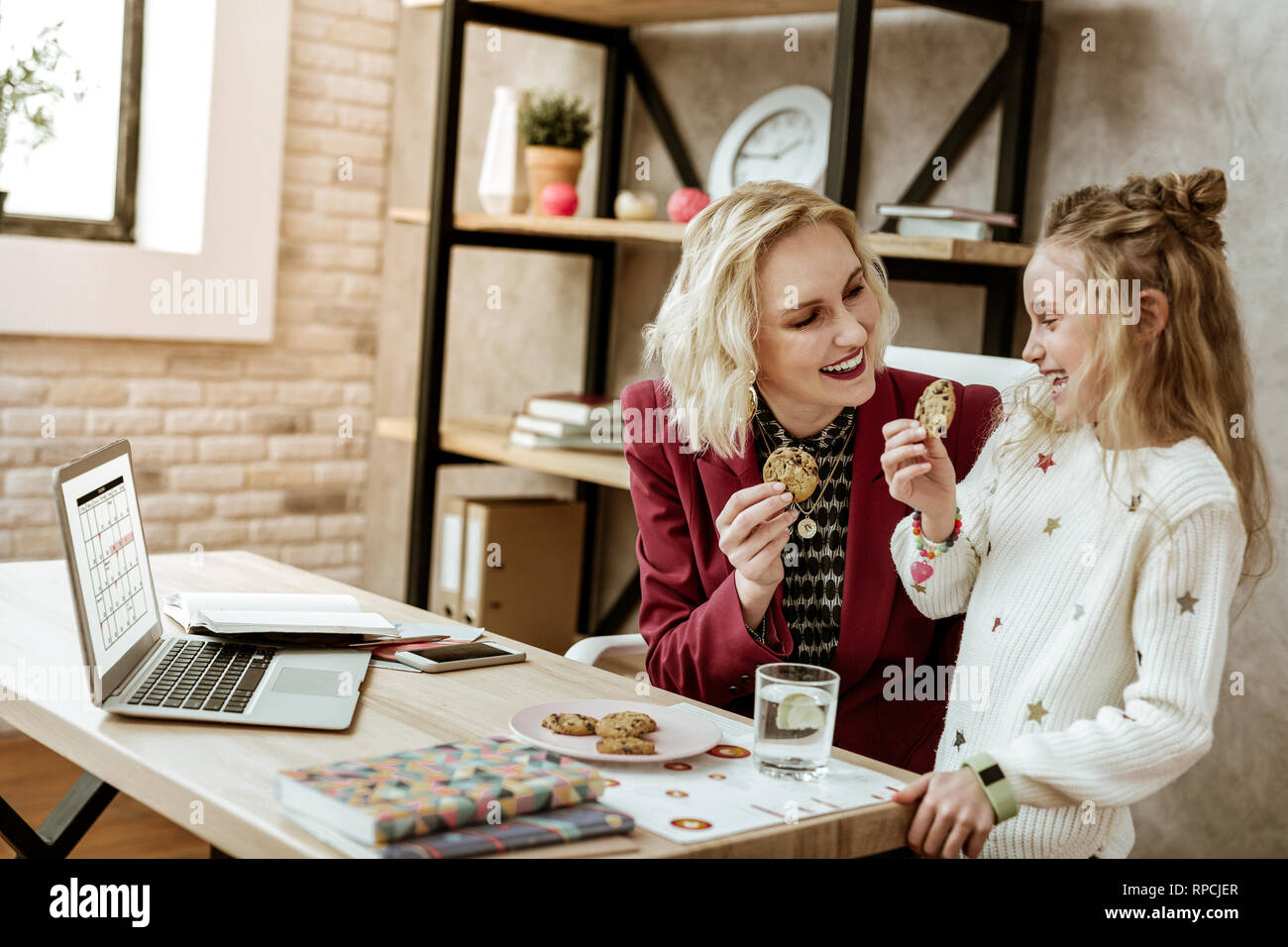 Cheerful positive mother carrying cookie and looking on her laughing ...