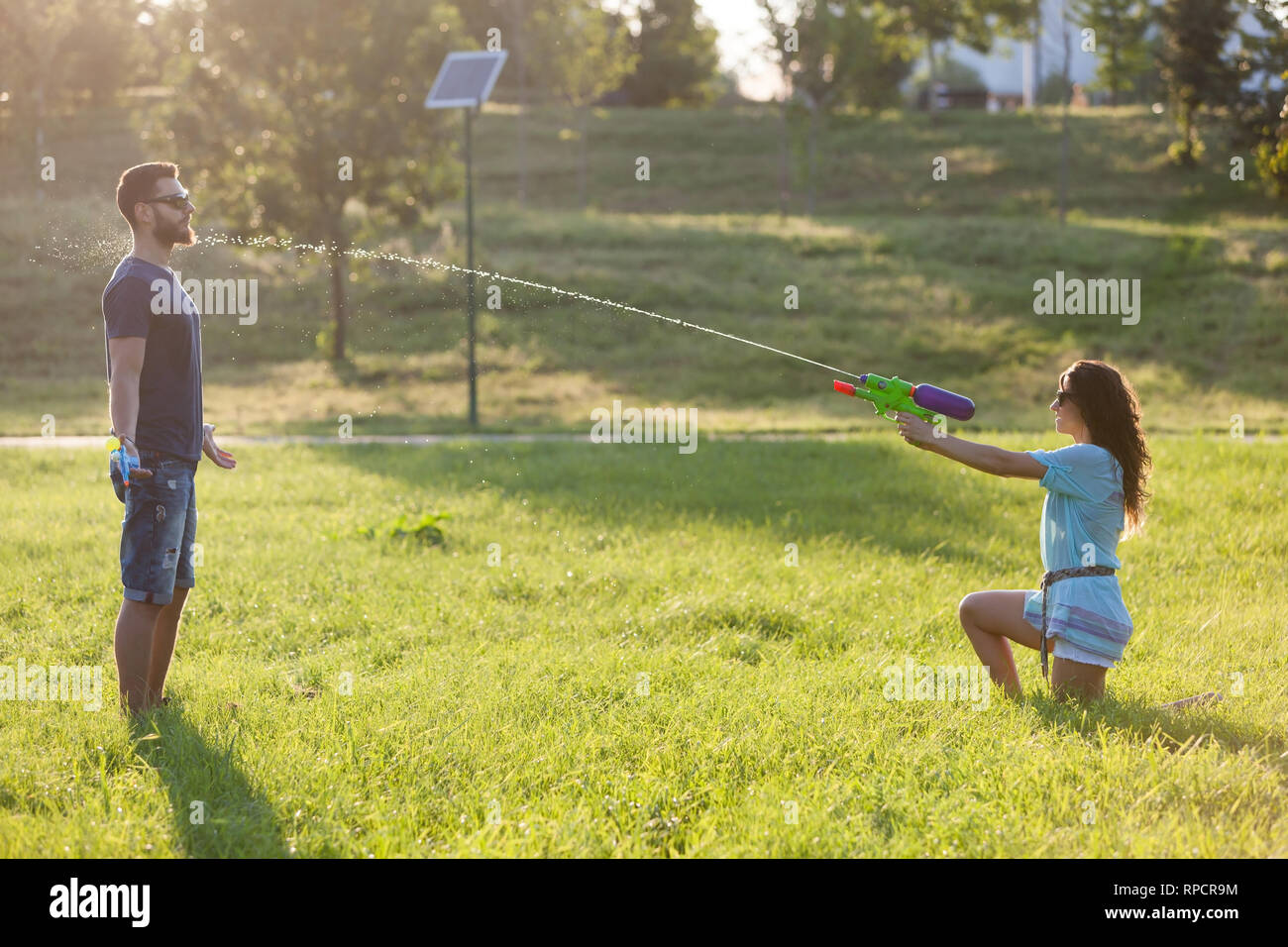 A playful young couple chasing each other and playing with water guns ...