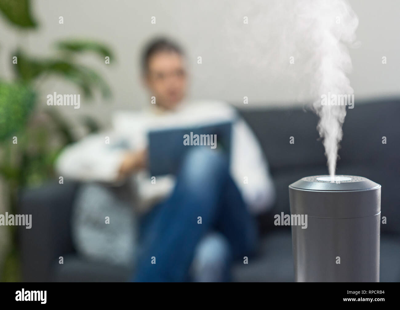 Air humidifier at living room. Man reading book on the background Stock ...