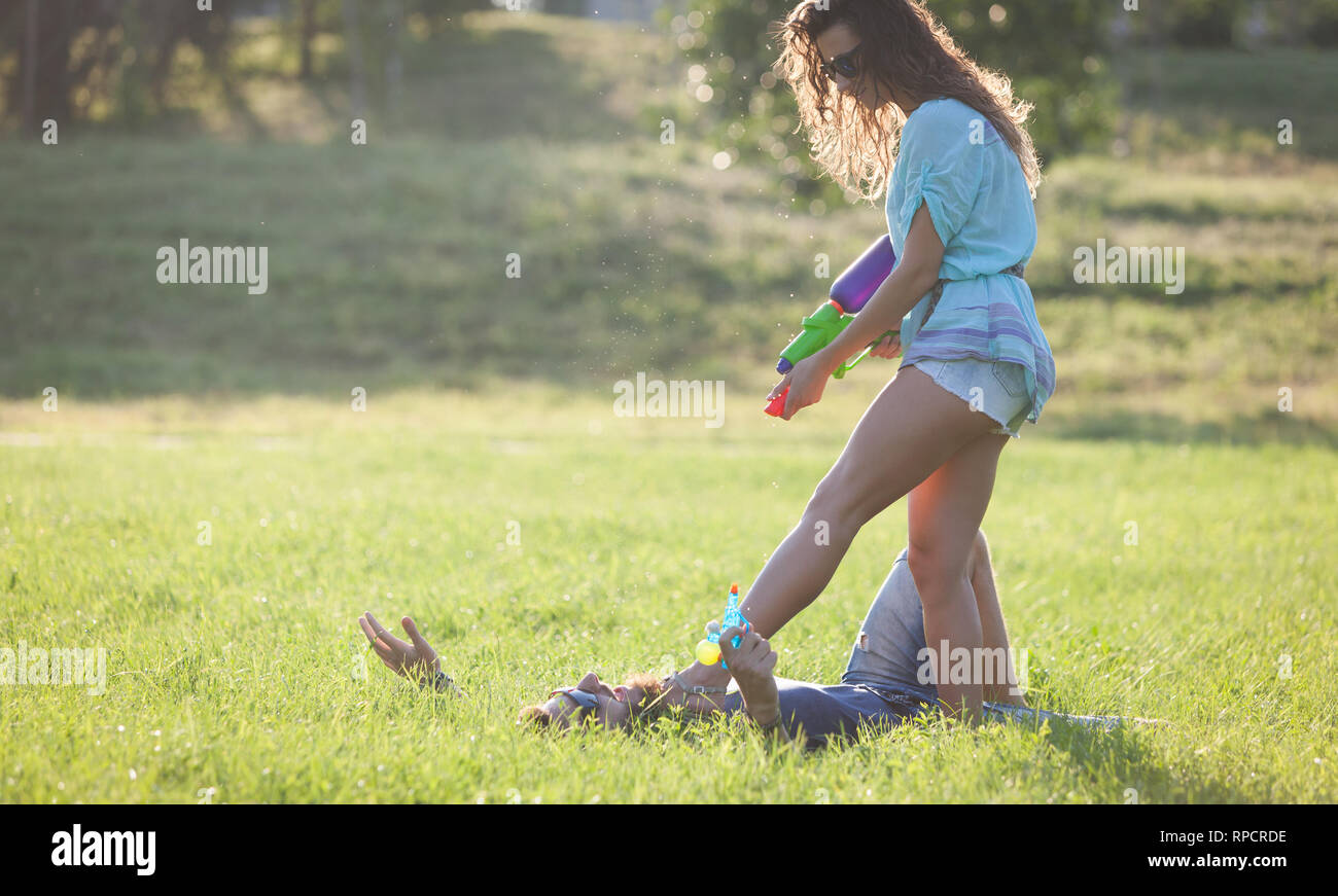 A playful young couple chasing each other and playing with water guns ...