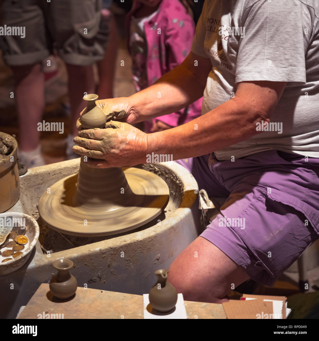 Potter makes a clay pot, sitting outside surrounded by people watching ...
