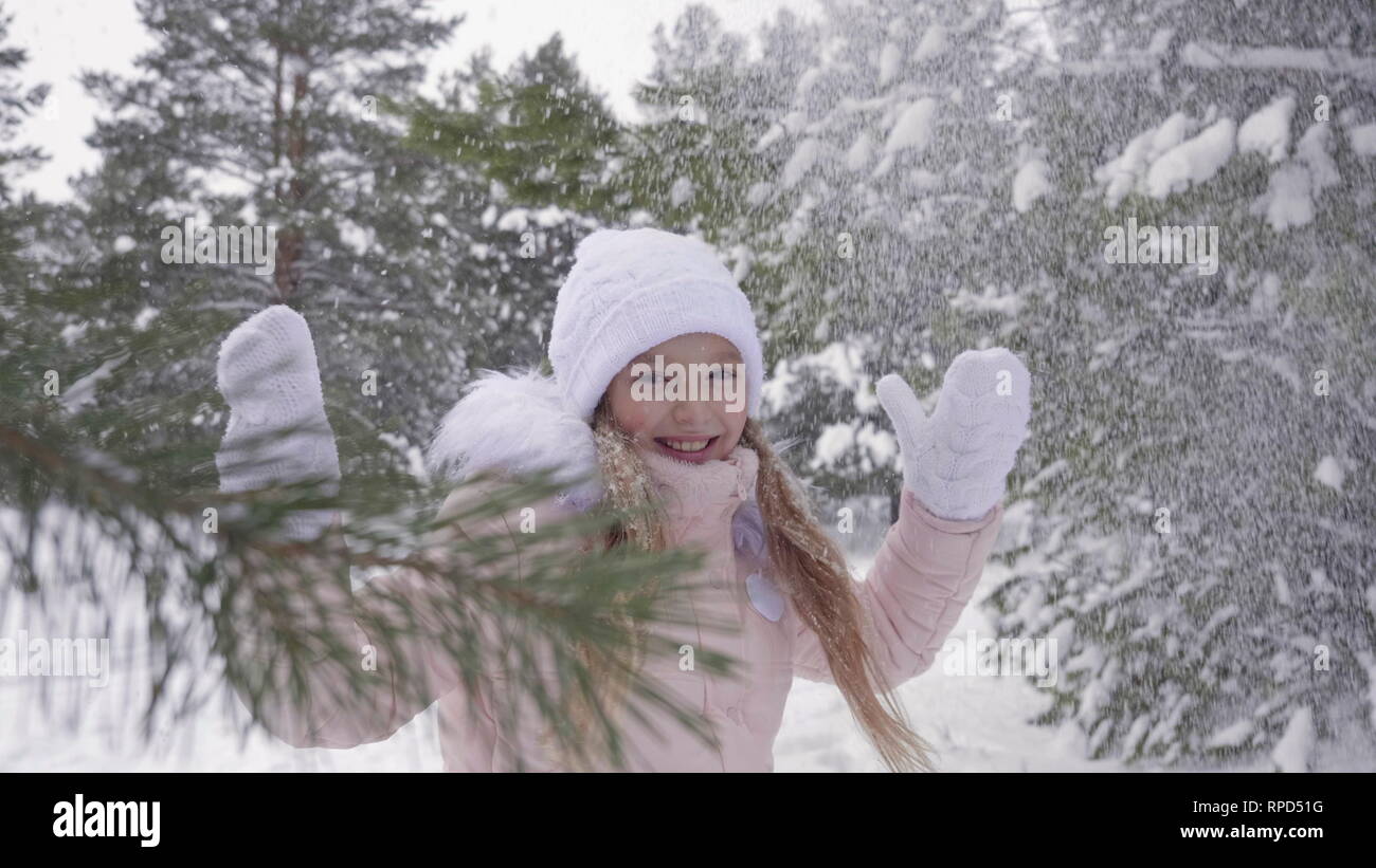 Beautiful teenager girl rejoicing winter snowfall in snowy forest slow ...